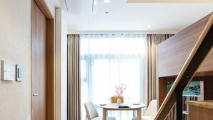 Quarto de hotel moderno com piso de madeira, área de refeições com mesa e cadeiras, e escada com corrimão de madeira.