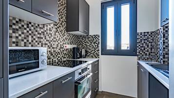 Cozinha compacta com micro-ondas, fogão e chaleira. Há uma janela com vista para edifícios.