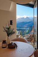 Uma varanda com vista para montanhas, uma mesa redonda com cadeiras e um vaso com plantas.