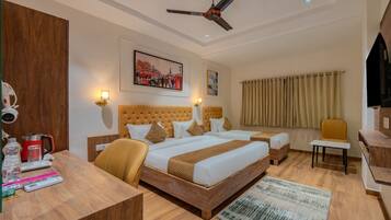 Quarto de hotel com uma cama grande, duas mesas de cabeceira, uma escrivaninha, uma cadeira, um ventilador de teto e uma televisão.
