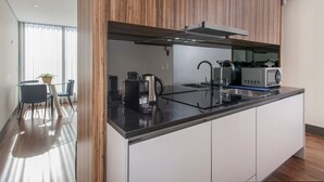Cozinha moderna com bancada preta, eletrodomésticos de aço inoxidável e painéis de madeira.