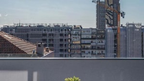 Um terraço no telhado com uma mesa de madeira e duas cadeiras, uma planta em vaso e uma almofada vermelha em cada cadeira.