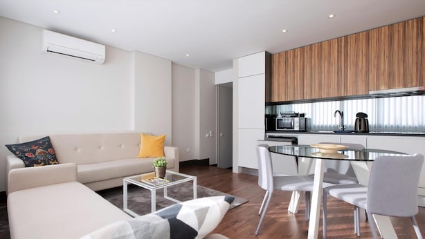Uma sala moderna com sofá, mesa de centro e área de jantar com cadeiras e mesa de vidro.