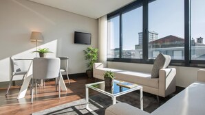 Uma sala de estar moderna com um sofá, uma mesa de centro, uma televisão e janelas amplas.