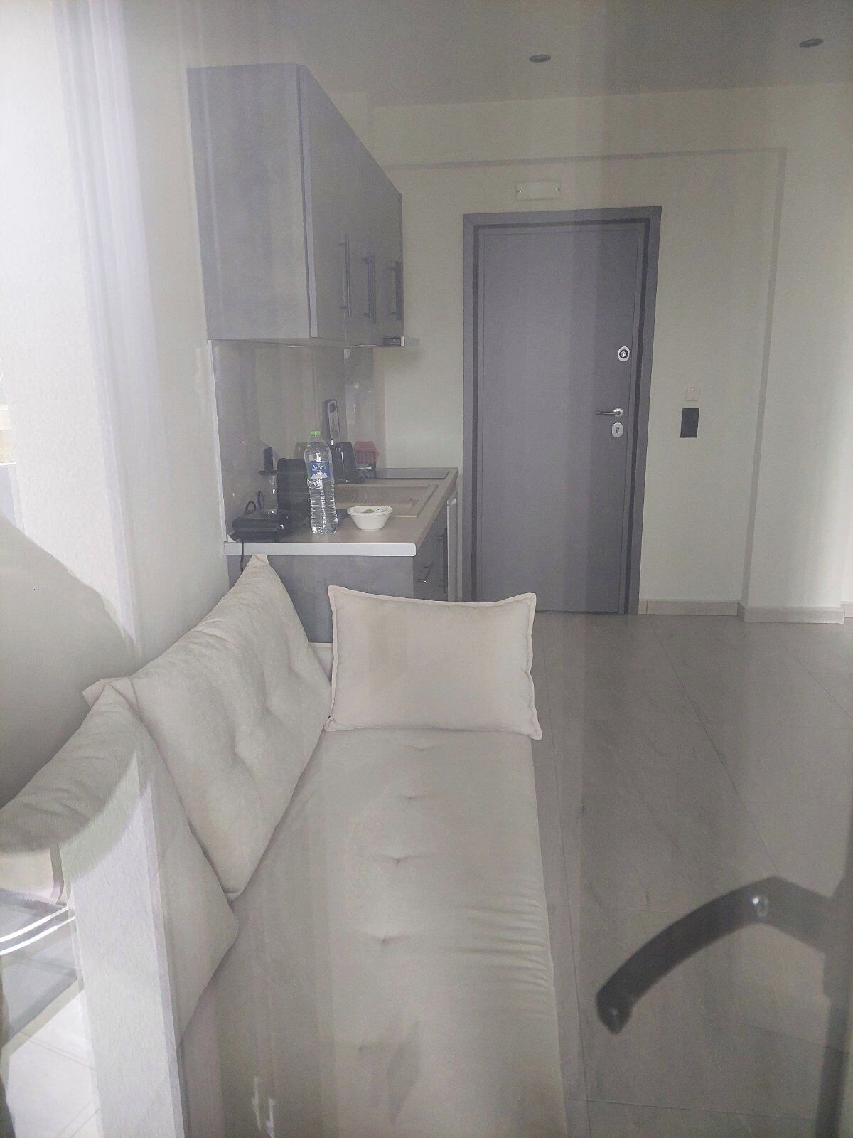 Quarto de hotel moderno com sofá, uma pequena mesa com uma garrafa e uma porta.