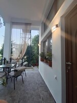 Uma área de estar coberta ao ar livre, com mesa, cadeiras, plantas em vasos e vista para os arredores.