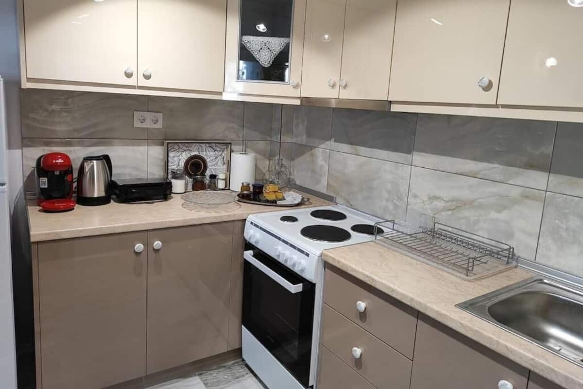 Uma cozinha compacta com armários bege, um fogão branco e uma pia de aço inoxidável.