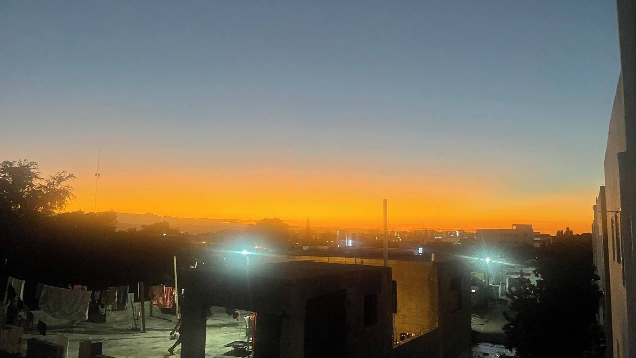 Vista de um horizonte urbano ao entardecer, com edifícios e postes de luz.
