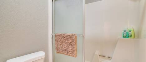 Casa de banho com sanita, cabine de duche em vidro e lavatório com artigos de higiene.