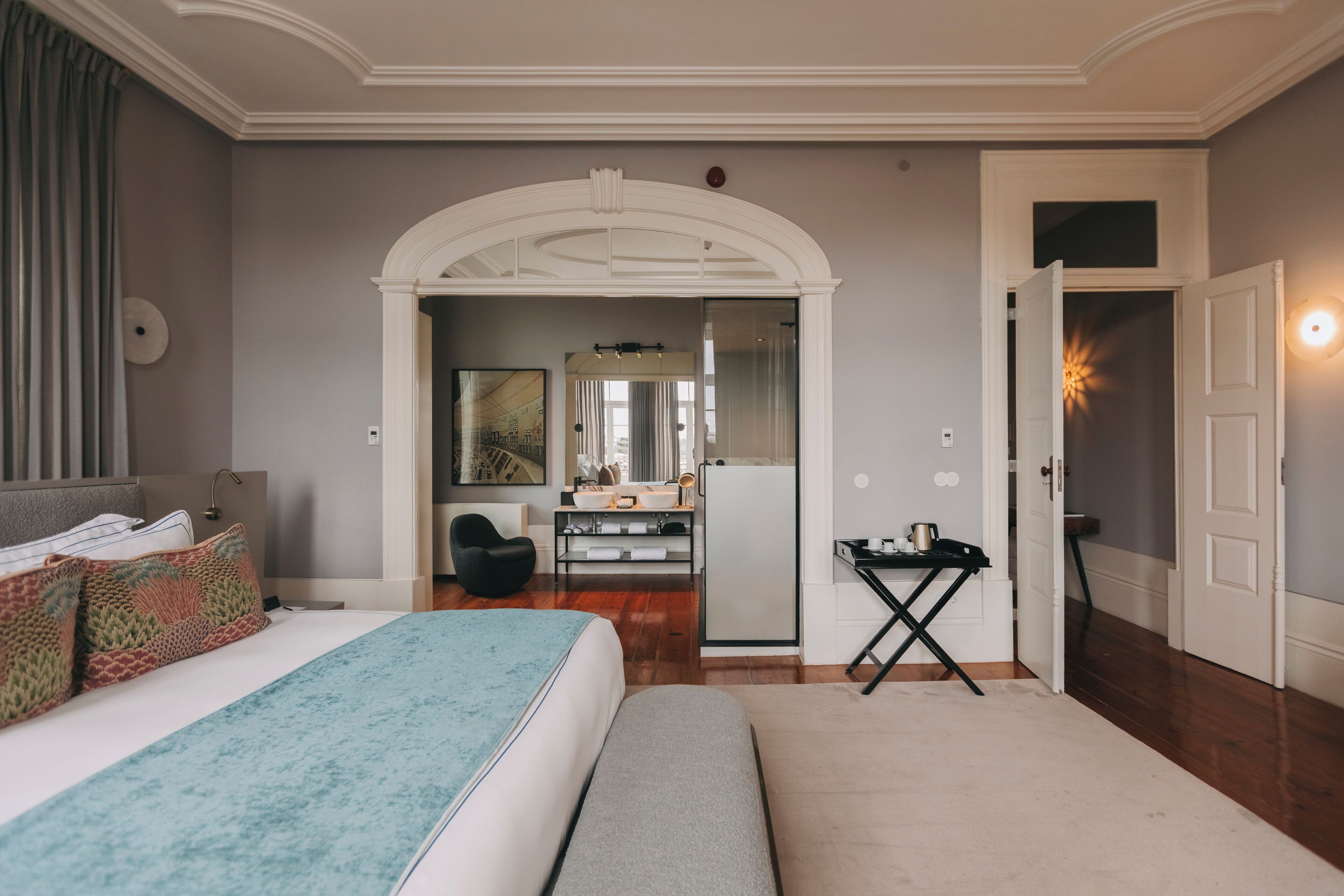 Quarto de hotel moderno com uma cama grande, uma escrivaninha, um espelho e uma kitchenette pequena.
