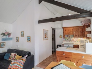 Sala de estar com sofá de couro preto, mesa de jantar de madeira e cozinha com armários de madeira e painel de azulejos.