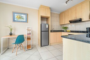 Uma cozinha moderna com armários de madeira, geladeira embutida, bancada e um espaço de refeições com uma cadeira e um vaso de flores.
