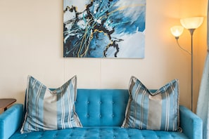 Um sofá azul com almofadas listradas, uma pintura abstrata moderna e um abajur.
