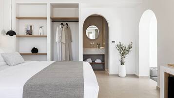 Quarto moderno com cama grande, estantes embutidas, closet espaçoso, banheiro com espelho e pia, e uma planta em vaso.