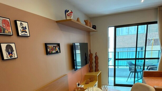 Uma área de jantar com mesa de madeira posta para quatro pessoas, um banco e uma TV fixada na parede.