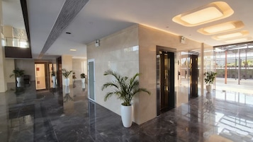 Um lobby moderno com piso de mármore polido, plantas grandes em vasos e entrada de vidro.