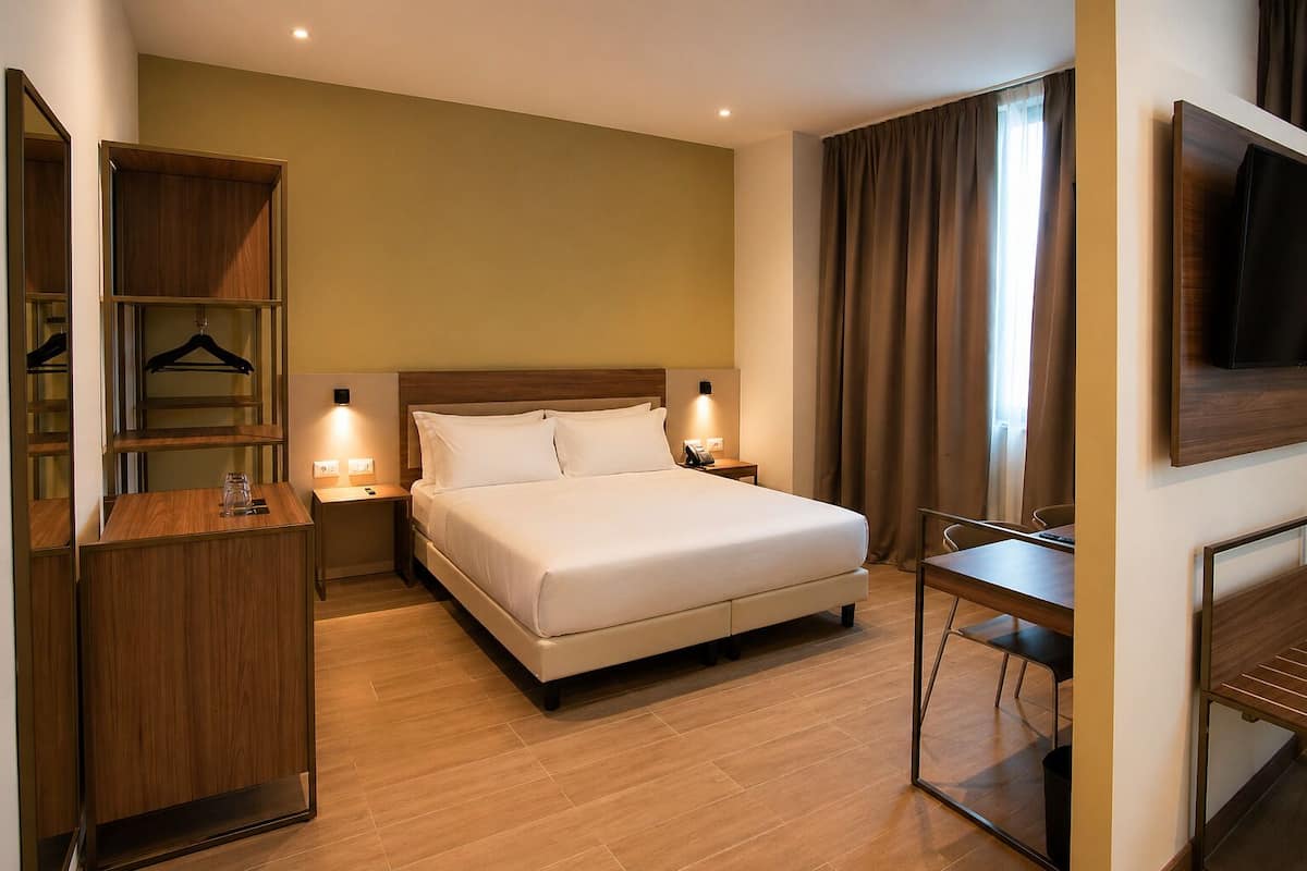 Quarto de hotel com cama, mesas de cabeceira, escrivaninha, televisão e guarda-roupa.
