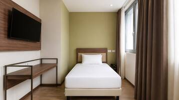 Quarto de hotel com uma cama, televisão na parede, escrivaninha e janela com cortinas.