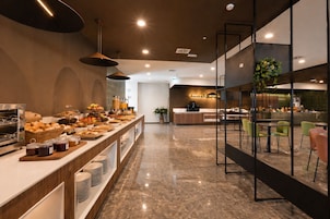 Um buffet de café da manhã moderno com diversas opções de alimentos, um espaço para café e uma área de estar com cadeiras.