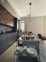 Uma cozinha moderna com armários cinza, uma ilha central com alimentos, e uma área de refeições com cadeiras.