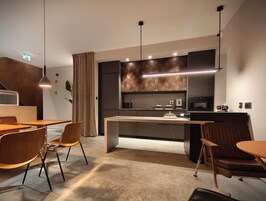 Uma cozinha moderna com ilha central, iluminação pendente e área de refeições com mobiliário de madeira.