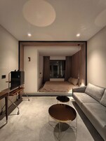 Quarto de hotel moderno com uma cama, um sofá, uma televisão sobre um suporte e uma mesa redonda pequena.