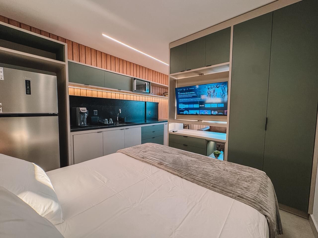Quarto de hotel compacto com cama, cozinha compacta e televisão.