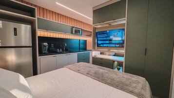 Quarto de hotel compacto com cama, cozinha compacta e televisão.