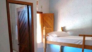 Um quarto com uma cama de solteiro, uma cama simples, uma porta de madeira e piso de azulejos.
