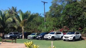 Uma área de estacionamento com vários SUVs, uma piscina pequena e gramado bem cuidado.