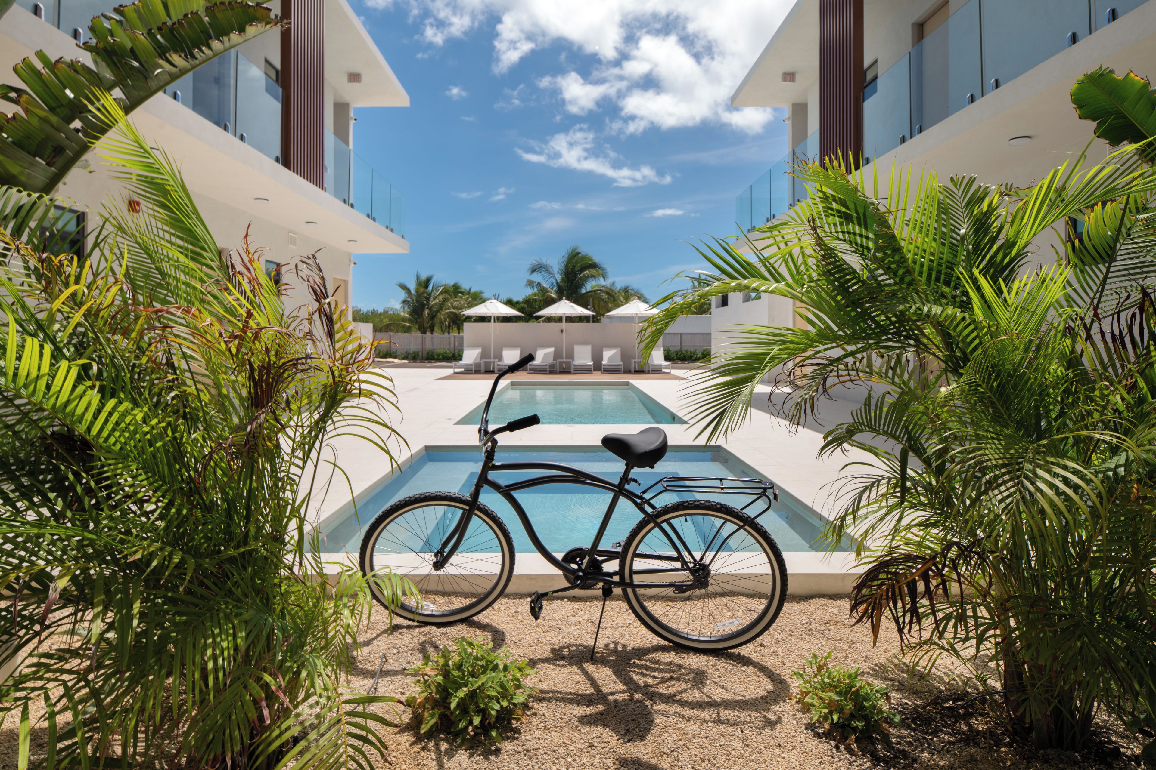 Bicicleta estacionada perto de uma piscina com cadeiras de sol e guarda-sóis ao fundo.
