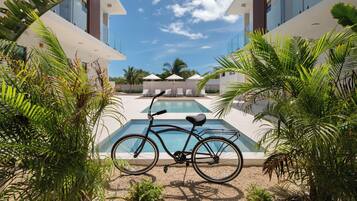 Bicicleta estacionada perto de uma piscina com cadeiras de sol e guarda-sóis ao fundo.