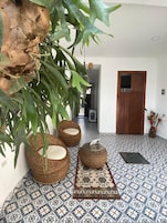 Quarto com piso de azulejos, uma planta grande, móveis de vime e um tapete estampado.