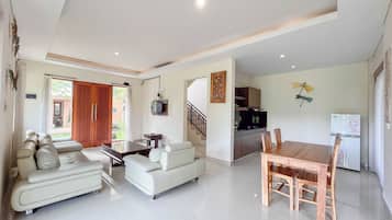 Uma sala de estar moderna com sofás, uma mesa de jantar com cadeiras, uma área de cozinha com geladeira e uma escadaria para outro andar.