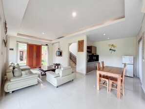 Uma sala de estar moderna com sofás, uma mesa de jantar com cadeiras, uma área de cozinha com geladeira e uma escadaria para outro andar.