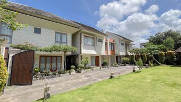 Um edifício residencial moderno com um caminho de entrada pavimentado, um gramado bem cuidado e diversos vasos de plantas e arbustos.