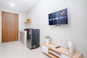 Cozinha moderna com geladeira, porta de madeira, prateleira pequena com uma planta e televisão de tela plana fixada na parede.