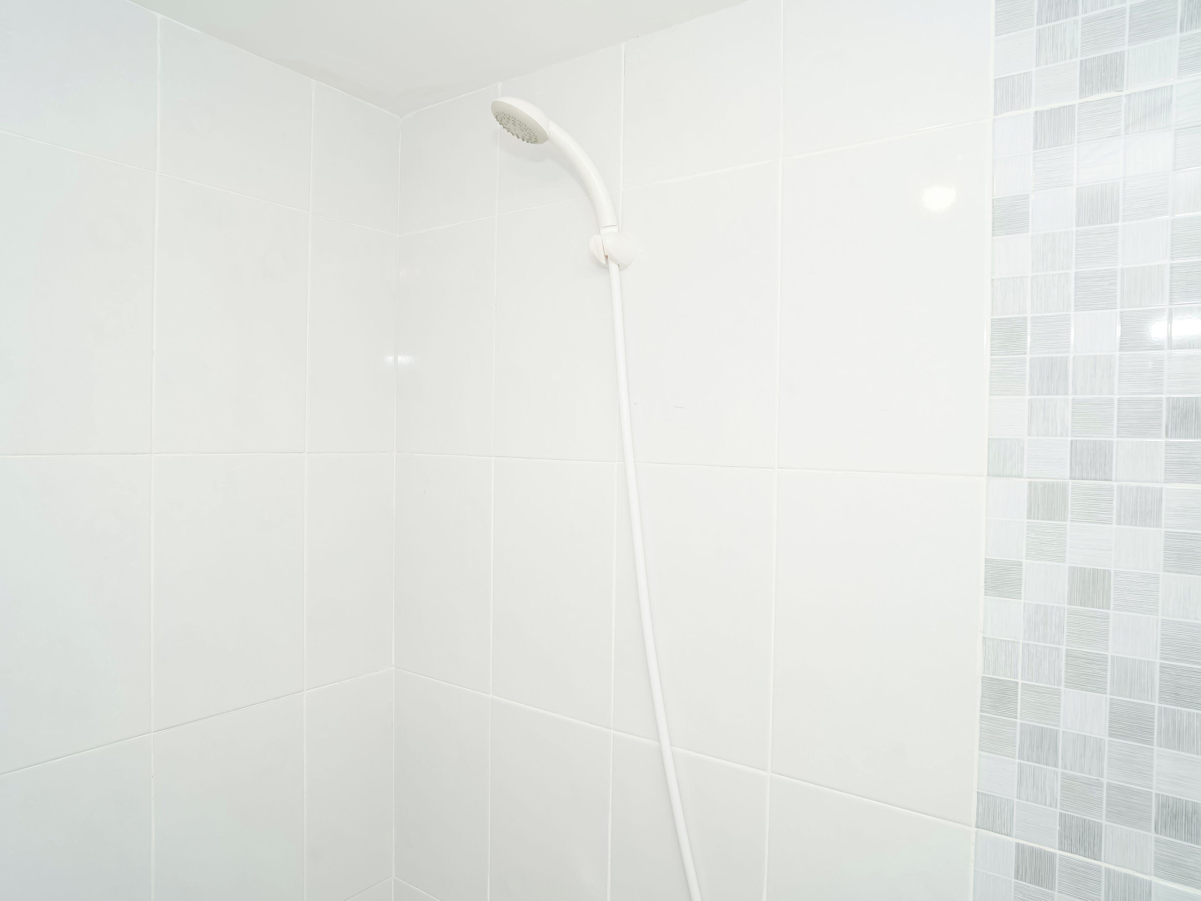 Um chuveiro com um chuveiro manual branco em um espaço com paredes revestidas de azulejos brancos.