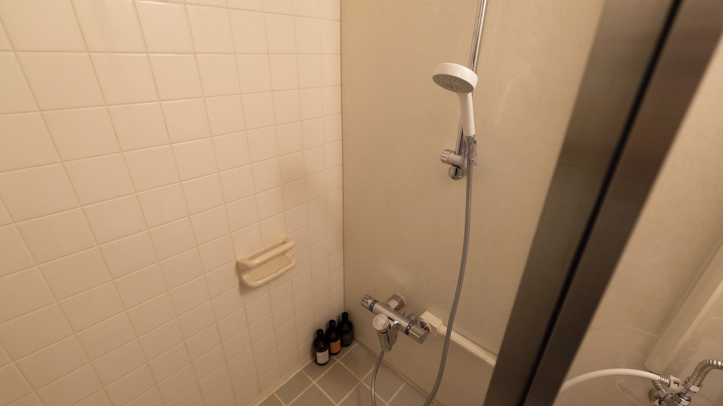 Um banheiro pequeno com azulejos, um chuveiro, um vaso sanitário e um corrimão.
