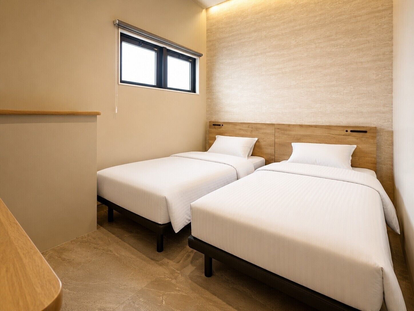 Quarto com duas camas de solteiro, uma janela e cabeceira de madeira.