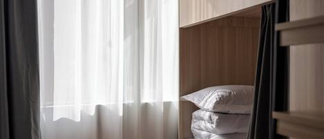 Quarto com cama beliche, cabeceira de madeira e cortinas leves.