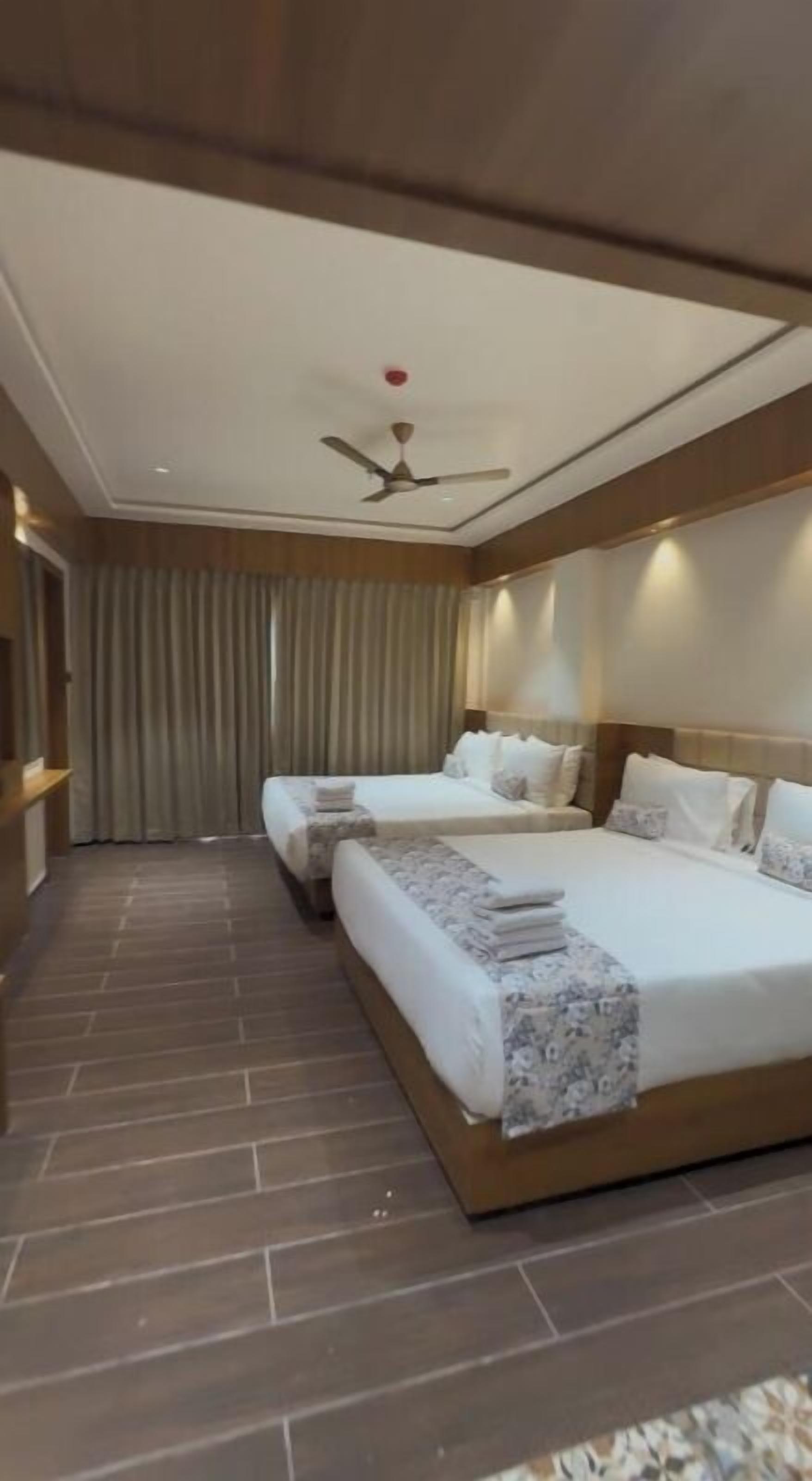 Quarto de hotel com uma cama grande, uma cama menor, um ventilador de teto e vista para a cidade pela janela.