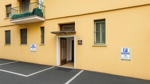 Um edifício amarelo com varanda, porta e duas placas de estacionamento.