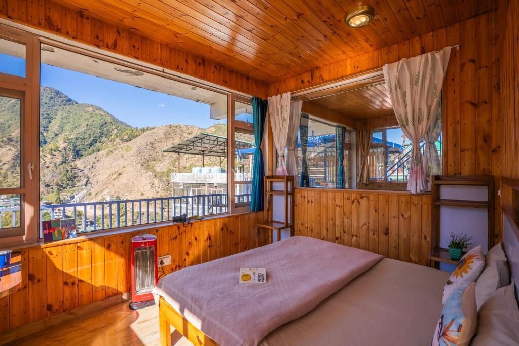 Uma cabana de madeira com cama, janela com cortinas e vista para montanhas.