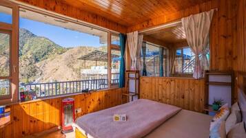 Uma cabana de madeira com cama, janela com cortinas e vista para montanhas.