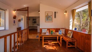Uma área de estar com bancos de madeira, uma mesa, um relógio na parede e uma janela com cortinas.