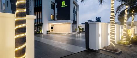 Entrada moderna de hotel com caminho bem iluminado, palmeiras e um edifício com a placa