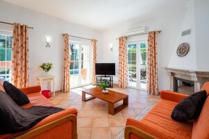 Sala de estar com sofás laranja, mesa de centro de madeira, televisão e lareira.