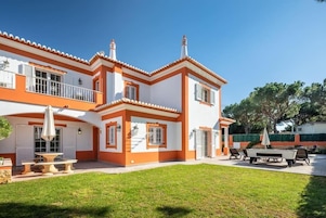 Uma casa de dois andares com um alpendre, mobiliário para área externa e um gramado bem cuidado.
