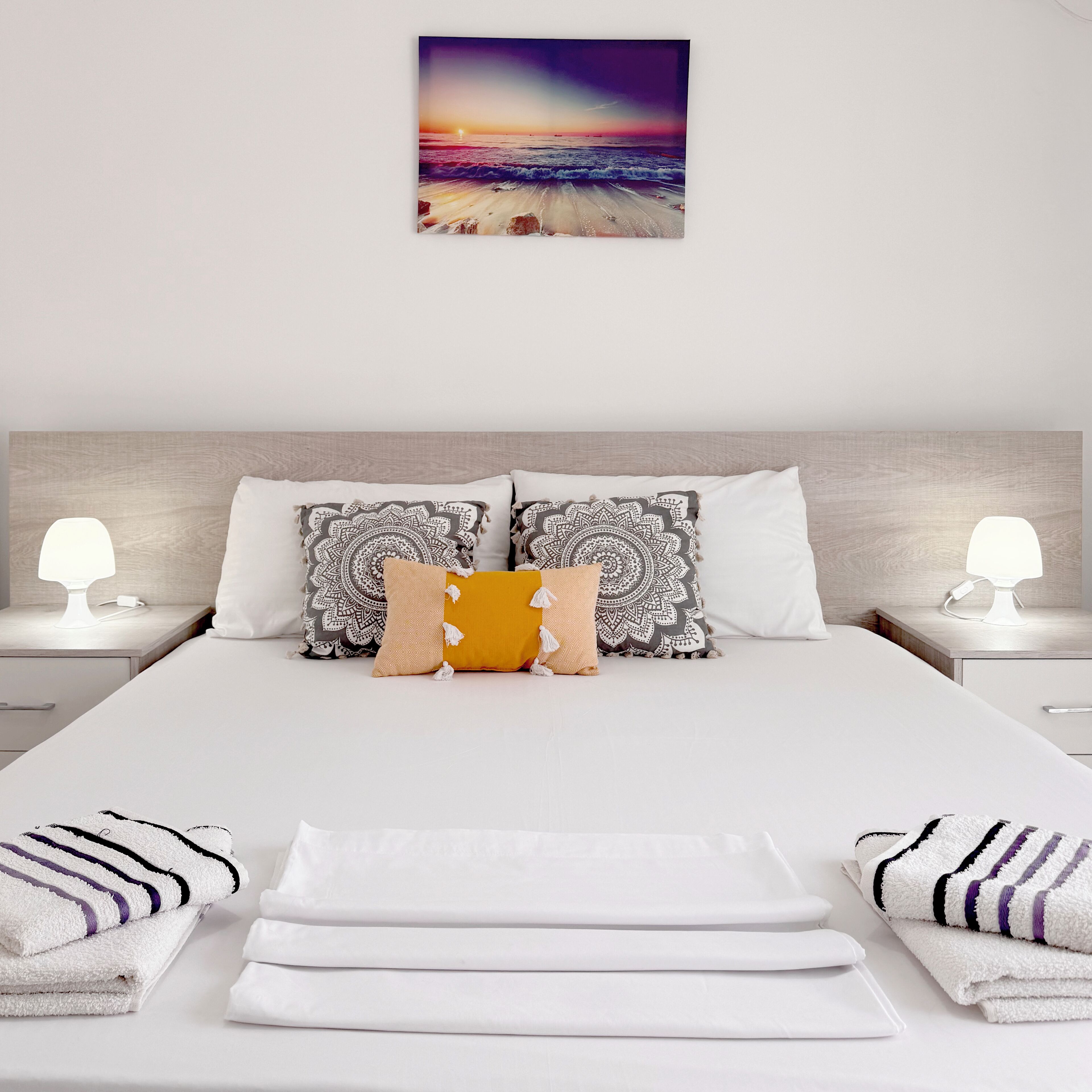 Cama bem arrumada com almofadas estampadas, toalhas brancas e abajures.
